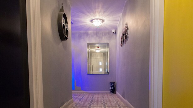 Um corredor com piso de ladrilhos estampados, teto com iluminação embutida e uma porta à direita.
