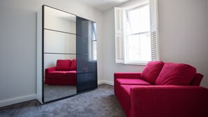 Um quarto com um sofá vermelho, um espelho grande e uma janela com persianas.