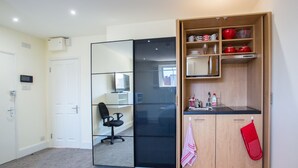 Quarto compacto com porta deslizante para um armário com espelho, cozinha compacta com armários de madeira e tapete vermelho.
