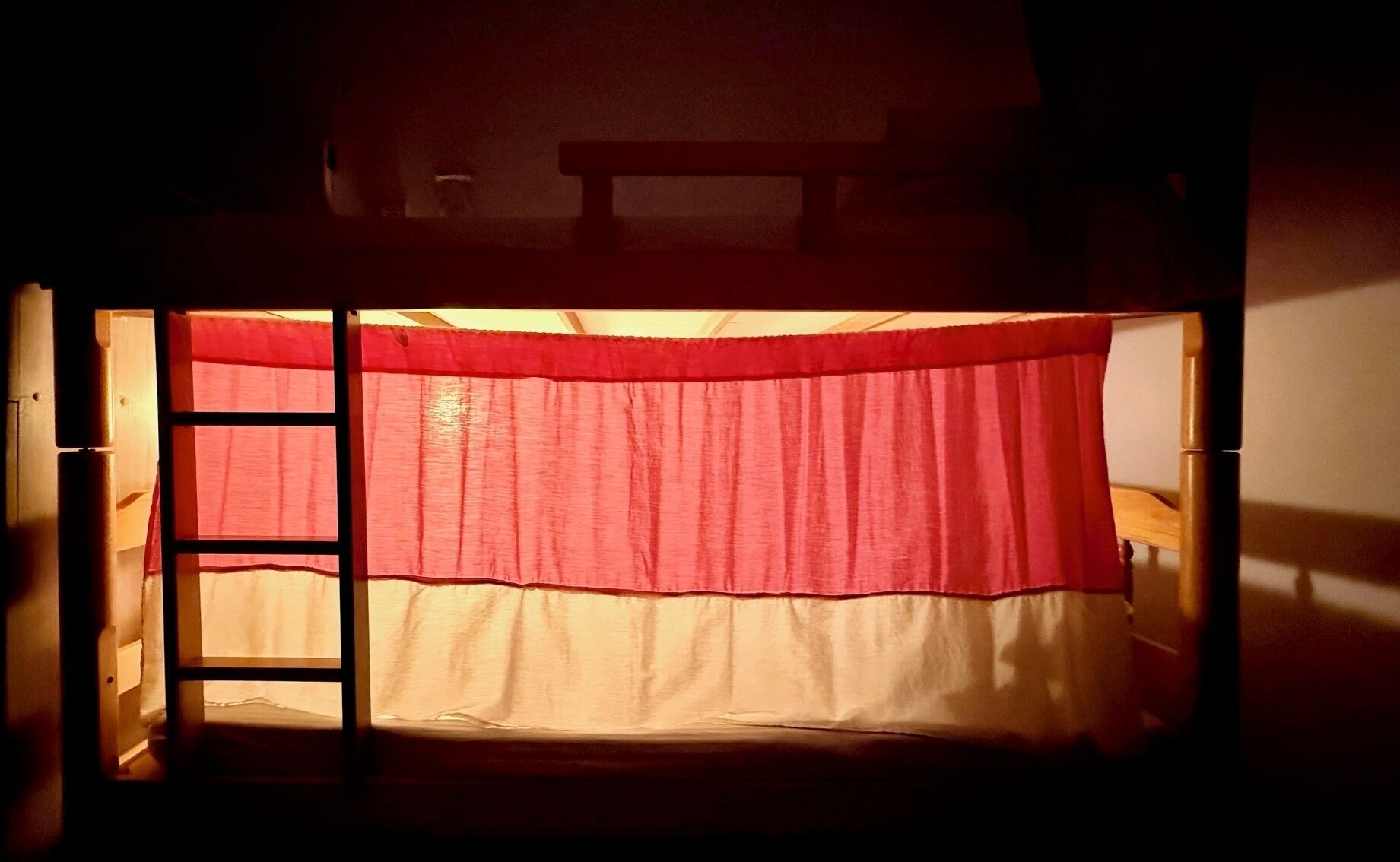 Uma cama beliche com cortina vermelha e escada.