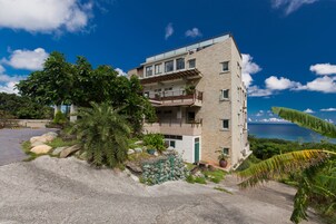 Um edifício de vários andares com varanda, rodeado por vegetação e vista para o oceano.