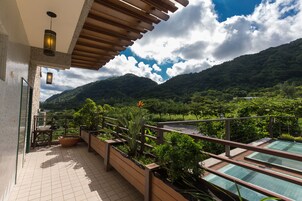 Varanda com vista para paisagem montanhosa, guarda-corpo de madeira e plantas em vasos.