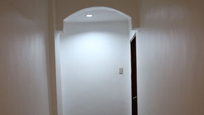 Um corredor estreito com chão de azulejos e paredes brancas, que leva a uma porta no final.