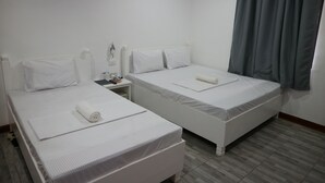 Quarto de hotel com duas camas de solteiro, uma mesinha de cabeceira com abajur e uma janela com cortinas.