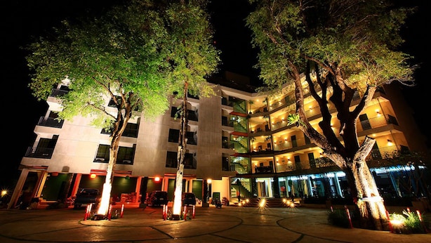 Um hotel de vários andares com um pátio, árvores e varandas iluminadas.