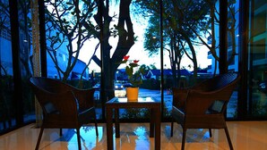 Decoração moderna com duas cadeiras de vime e uma mesa, janelas amplas com vista para árvores e edifícios, e piso refletivo.