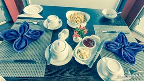 Mesa de café da manhã posta com pratos brancos, uma tigela de cereal, uma tigela de geleia e um pequeno vaso com flores.
