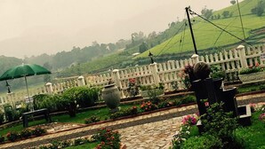 Caminho no jardim com piso de pedra, cercado por canteiros de flores e vegetação.