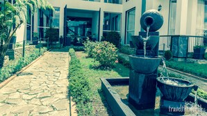 Um pátio com caminho de pedra, um elemento de água e um edifício com janelas amplas e varanda.