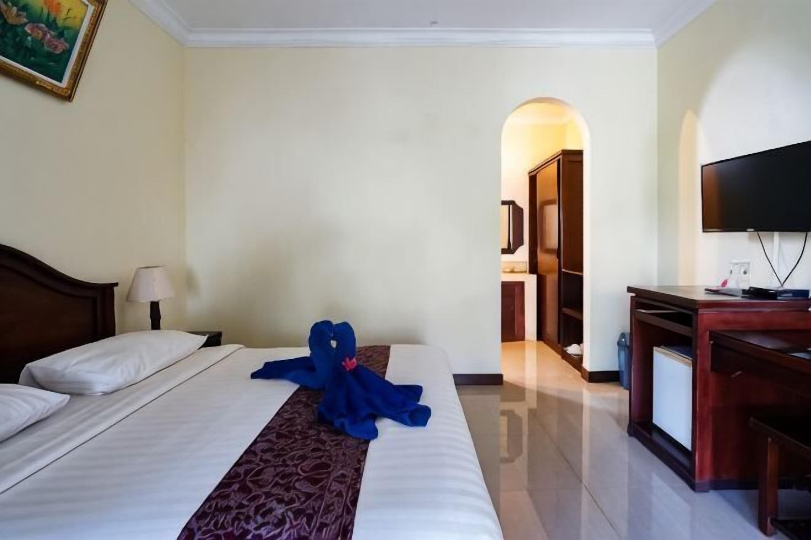 Quarto de hotel com cama, escrivaninha, televisão e banheiro visível por um arco.