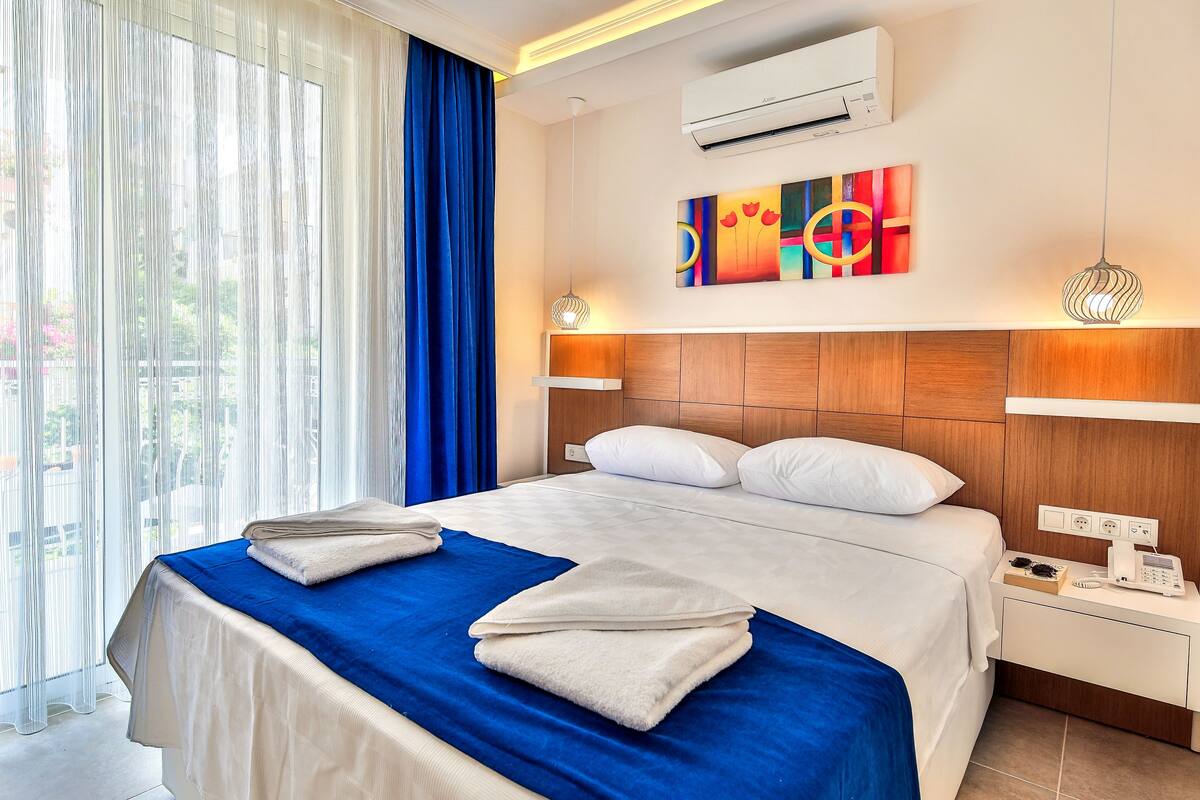 Quarto de hotel com cama, mesa de cabeceira, ar condicionado, um quadro e vista para o exterior.