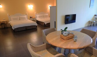 Quarto de hotel com duas camas, televisão, mesa de jantar com cadeiras e uma pequena mesa com chaleira e xícaras.
