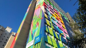 Um hotel alto com listras verticais coloridas e varandas, com uma placa indicando 'Mercure Hotel' e a marca 'Ibis Budget'.