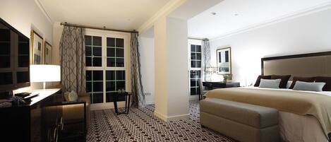 Quarto de hotel com cama, mesa de cabeceira, luminária e escrivaninha com cadeira.