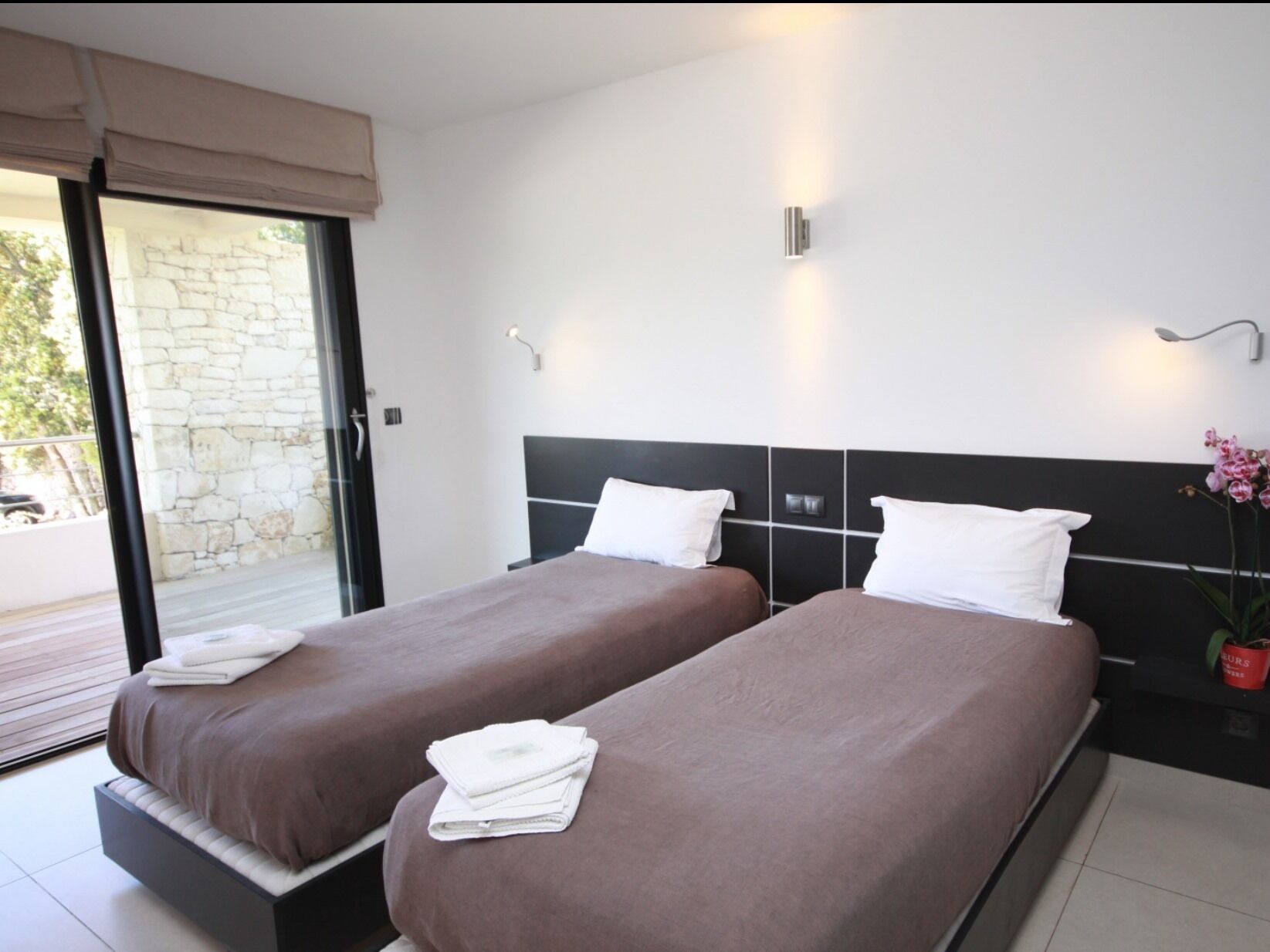 Quarto de hotel moderno com duas camas, uma parede de pedra e uma varanda.