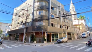 Hotel com fachada moderna, entrada visível e vista da rua com veículos e faixa de pedestres.
