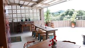 Um pátio externo com mesa e cadeiras de madeira, um painel decorativo e plantas em vasos.