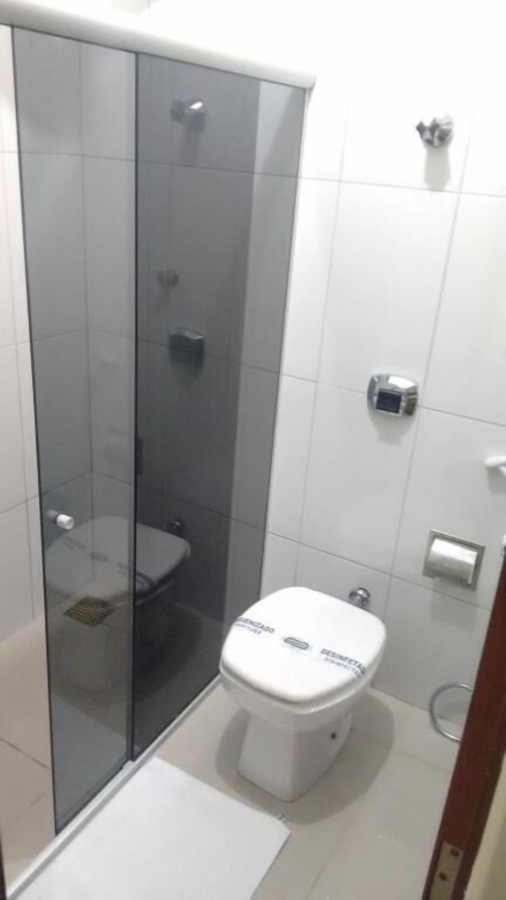 Casa de banho moderna com cabine de duche em vidro, sanita branca e secador de mãos à vista.