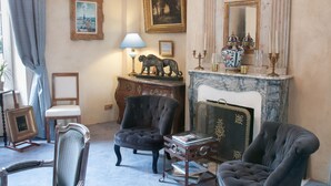 Quarto com lareira, dois poltronas, um armário de madeira e um quadro na parede.