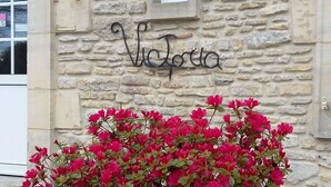 Um edifício de pedra com uma janela e uma placa que diz "Victoire". Em frente ao edifício, há um vaso grande com flores cor-de-rosa.