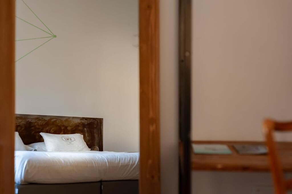 Quarto com cama, cabeceira de madeira e luminária fixada na parede.