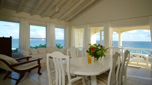 Uma área de refeições branca com uma mesa, cadeiras e vista para o oceano.