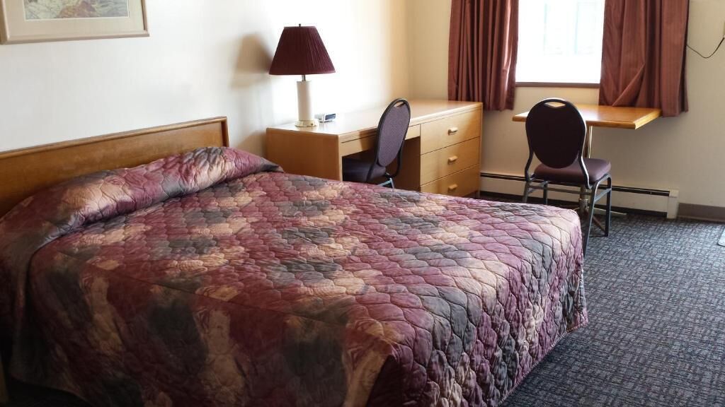 Quarto de hotel com uma cama grande, uma escrivaninha, uma cadeira e um abajur.