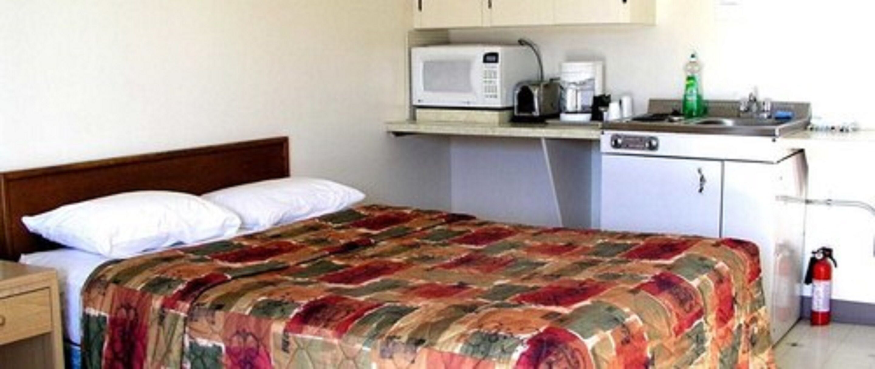 Um quarto pequeno e bem arrumado, com cama, micro-ondas, cafeteira e pia.