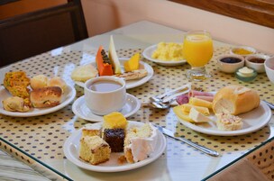 Uma mesa de café da manhã com diversos alimentos, incluindo doces, frutas e um copo de suco de laranja.