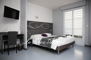 Quarto de hotel moderno com cama, escrivaninha, cadeira, televisão e janela com persianas.