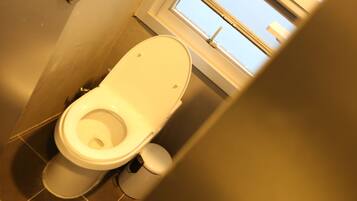 Sanitário com caixa de descarga, janela acima e chão ladrilhado.
