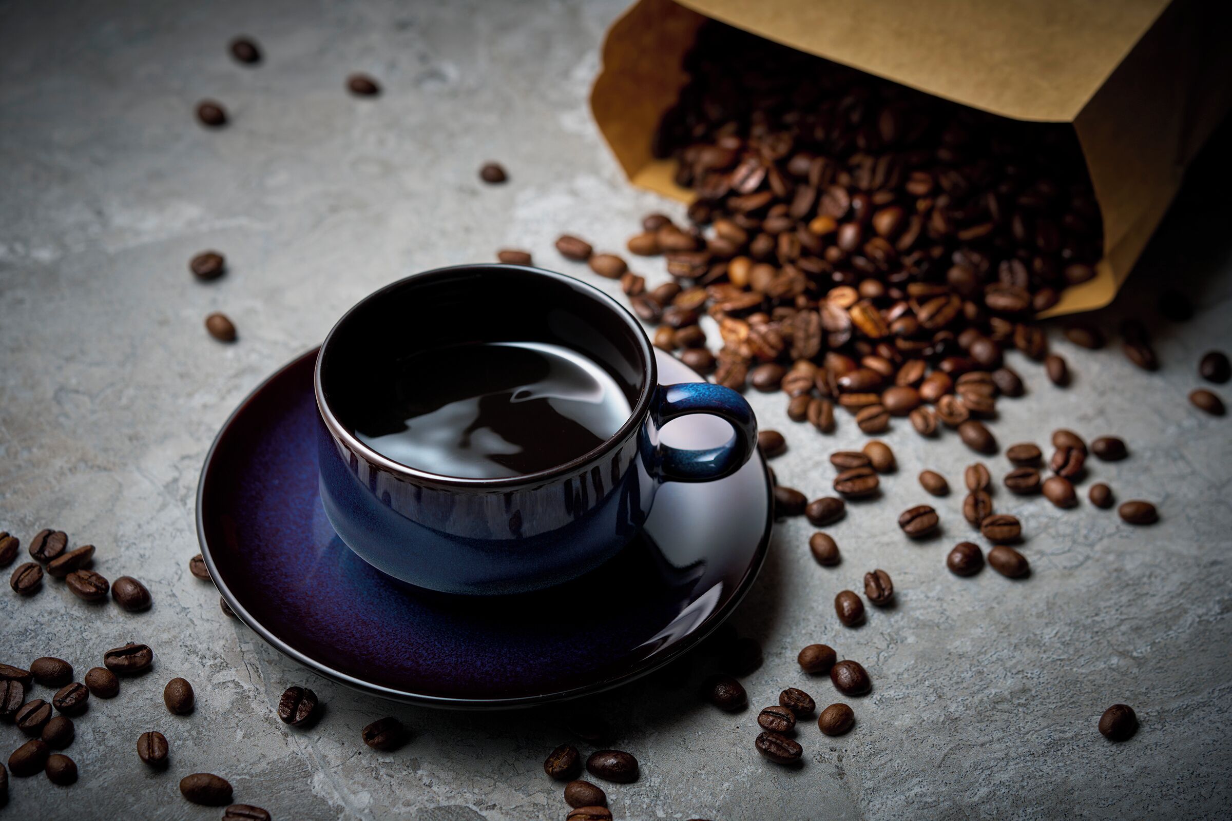 Uma chávena de café sobre um pires, com grãos de café espalhados à volta.