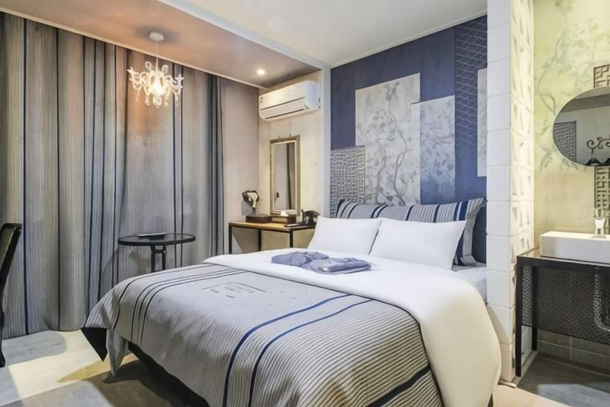Quarto de hotel com uma cama, uma escrivaninha, uma cadeira, um espelho e um banheiro.
