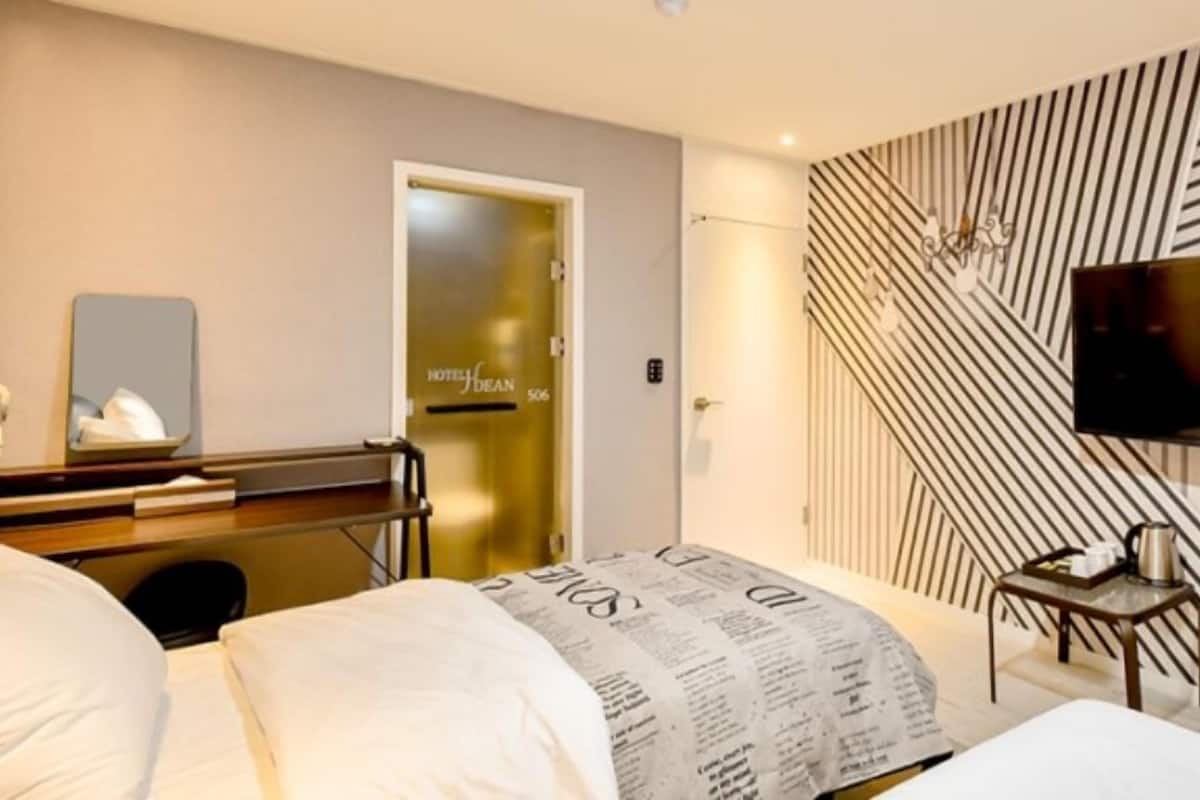 Quarto de hotel moderno com cama, mesa de cabeceira e televisão na parede.