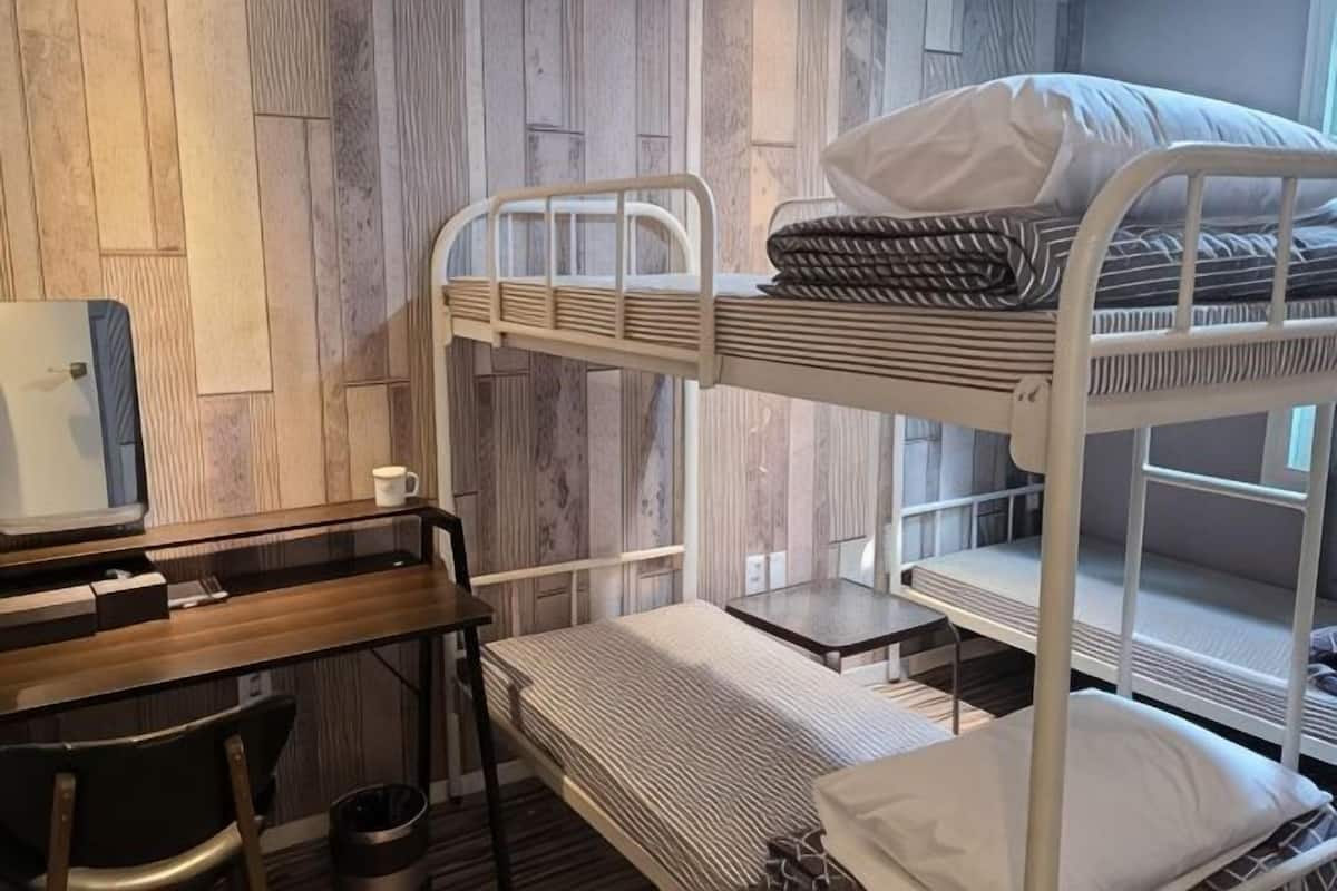 Quarto com beliche, escrivaninha, cadeira, mesa pequena e janela.