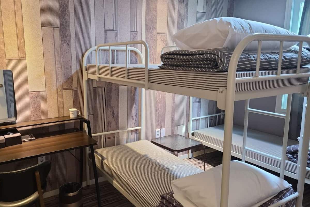 Quarto com beliche, escrivaninha, cadeira, espelho e janela.