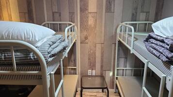 Quarto em dormitório com duas beliches, um banquinho pequeno e lambris de madeira.