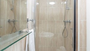Uma casa de banho moderna com cabine de chuveiro em vidro, prateleira de vidro e paredes revestidas a azulejos bege.