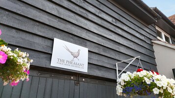Placa do pub e hotel 'The Pheasant', com ilustração de um frango e cestos de flores penduradas.