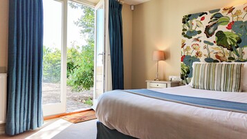 Quarto com cama, mesa de cabeceira, luminária e vista através de uma porta de vidro.