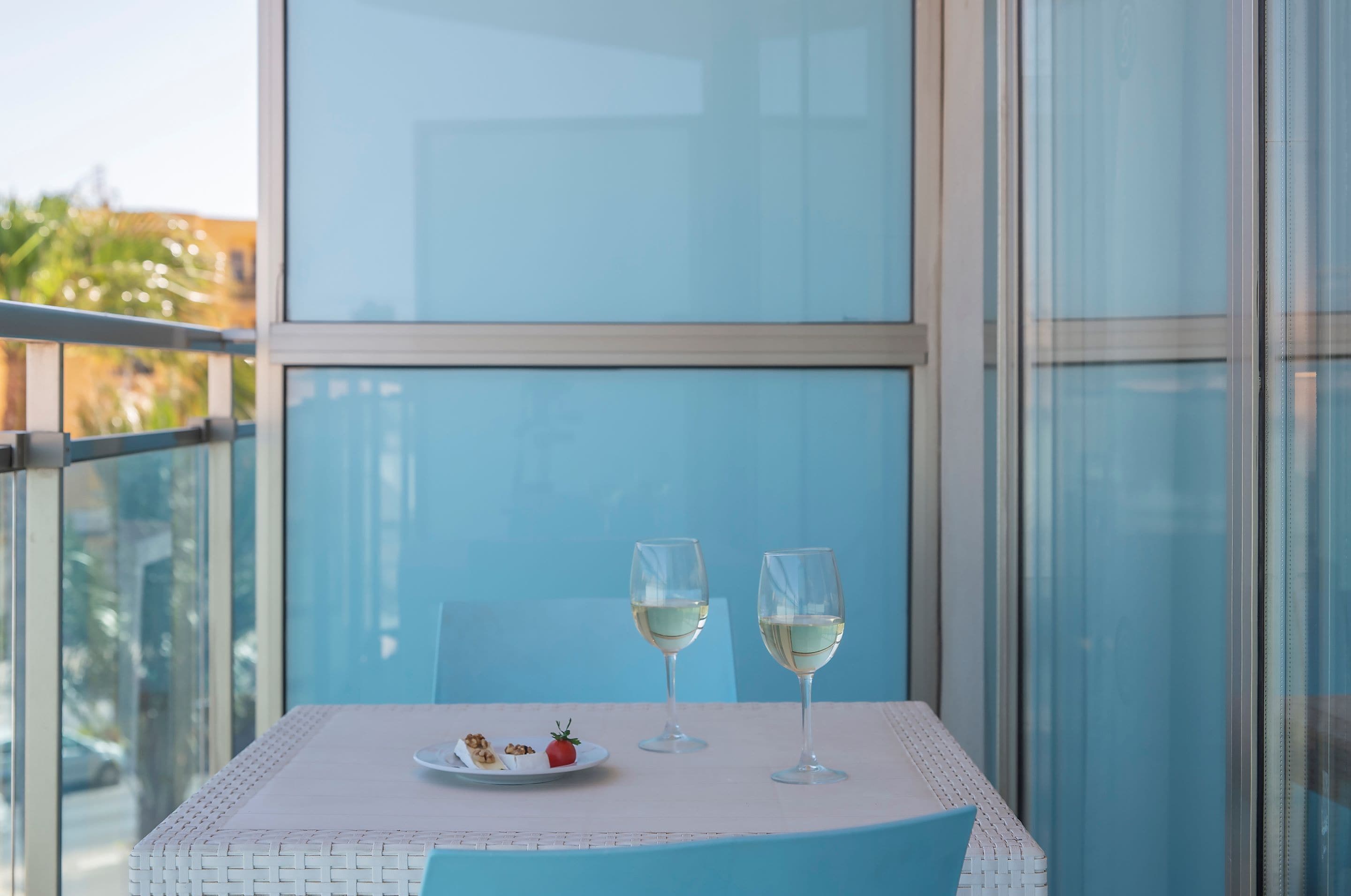Mesa com duas taças de vinho e um prato com comida numa varanda com vista para edifícios.