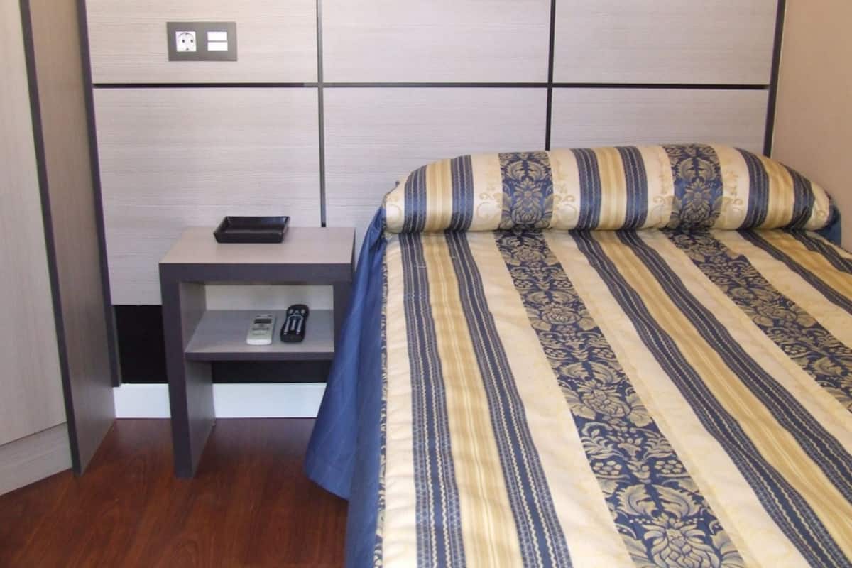 Quarto com cama, mesa de cabeceira e tomada na parede.