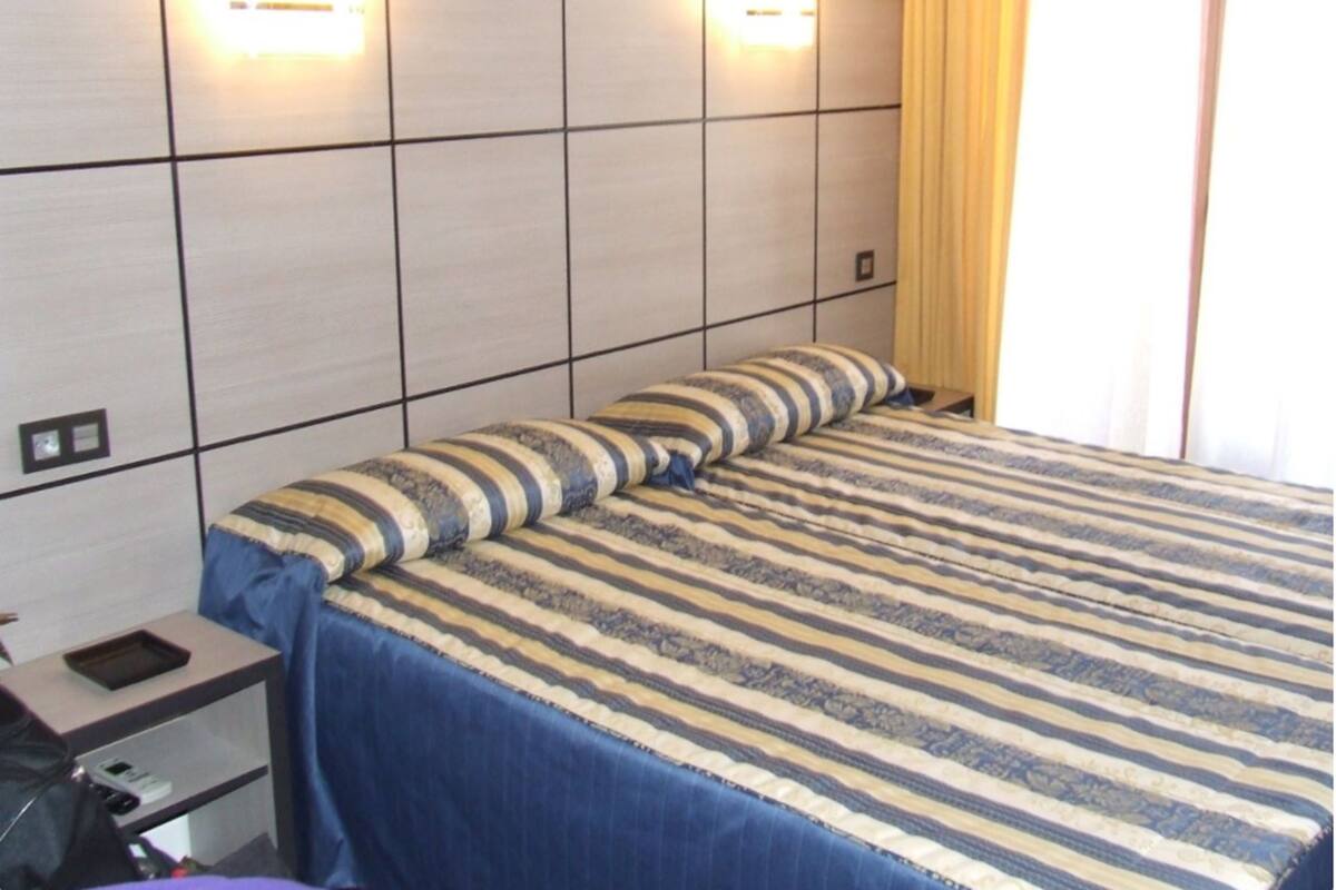 Quarto de hotel com uma cama, mesa de cabeceira e duas luzes na parede.