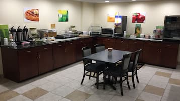 Cozinha com ilha central, mesa de jantar com cadeiras e diversos eletrodomésticos e utensílios.