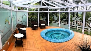 Uma área externa envidraçada com hidromassagem, móveis de vime e piso de madeira.