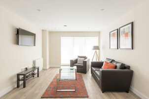 Uma sala de estar moderna com uma mesa de centro de vidro, um sofá preto e uma poltrona cinza.