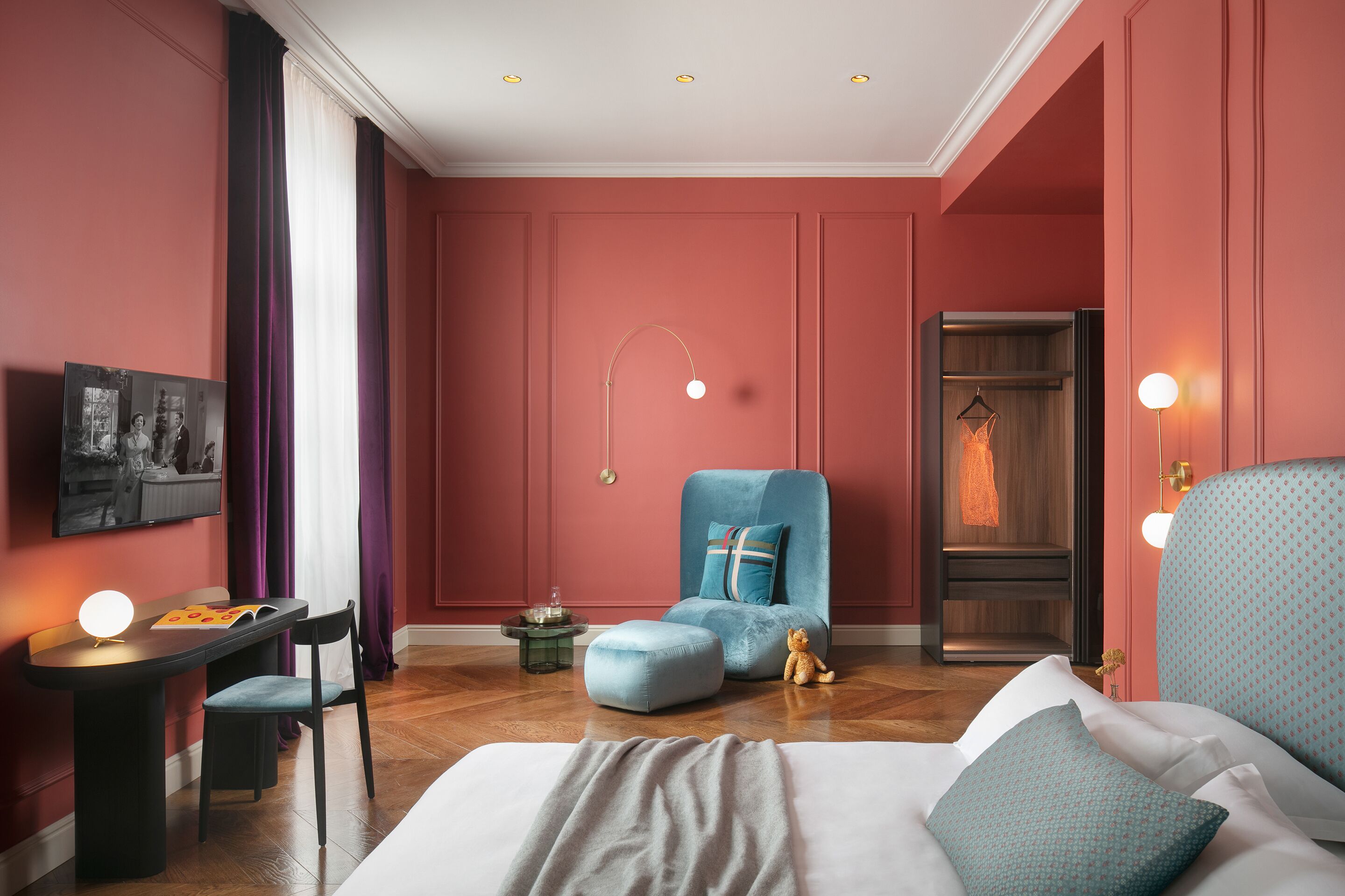 Quarto com cama, escrivaninha, cadeira, poltrona azul e luminária pendente.