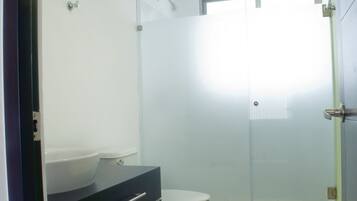 Uma casa de banho moderna com cabine de duche em vidro, sanita branca e toucador escuro.