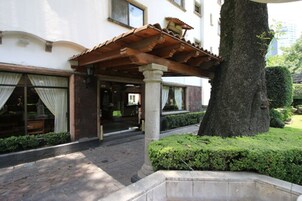 Um edifício com entrada coberta, uma grande árvore e um jardim bem cuidado.