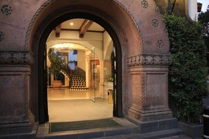 Uma entrada em arco com uma escadaria que leva ao interior, um lustre e um vaso de plantas.